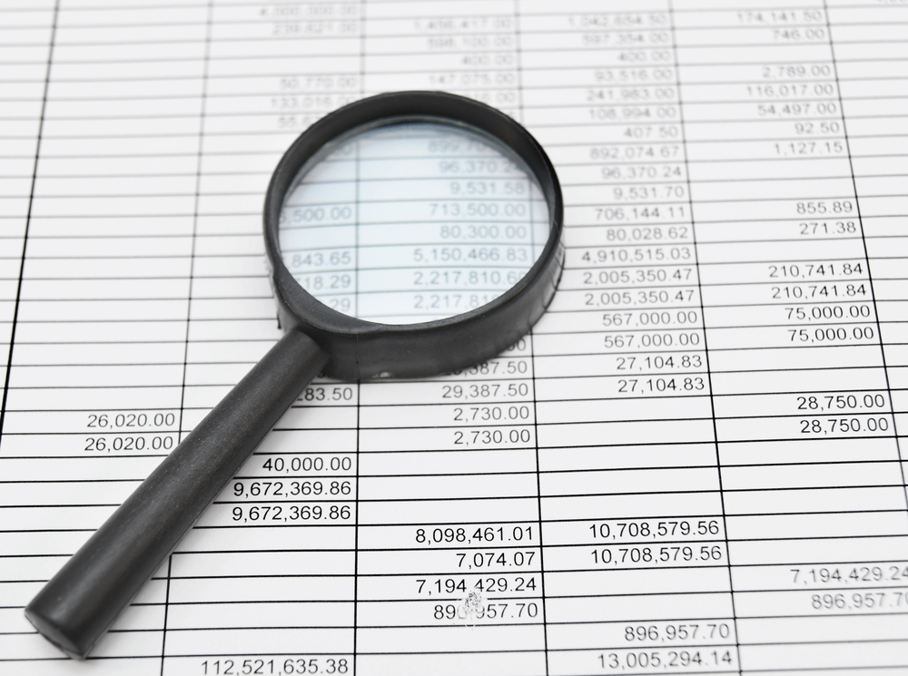 magnifying glass on spreadsheet - Money Nation